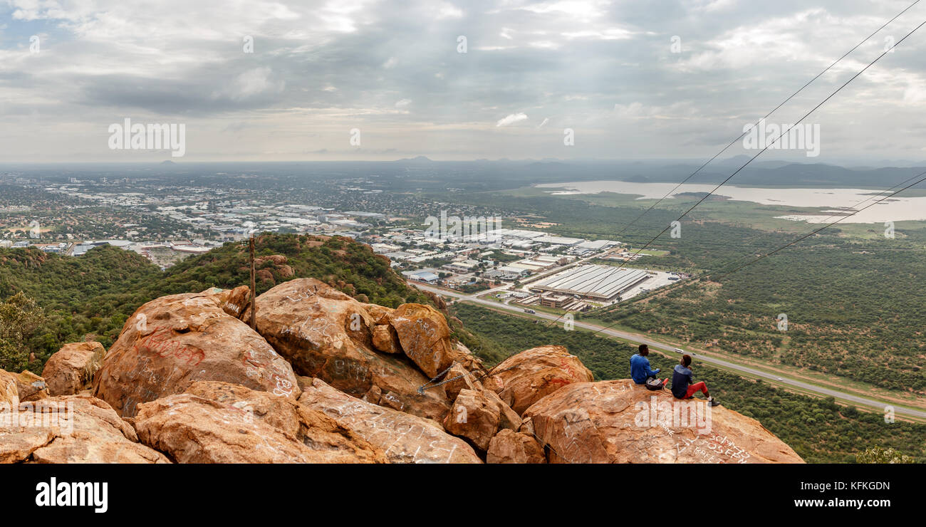 People sitting on the stones on the mountain with Gaborone city ...