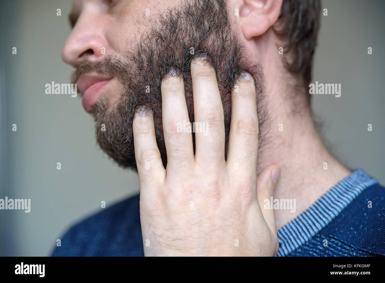 Close-up of young bearded man touching his beard while standing against ...