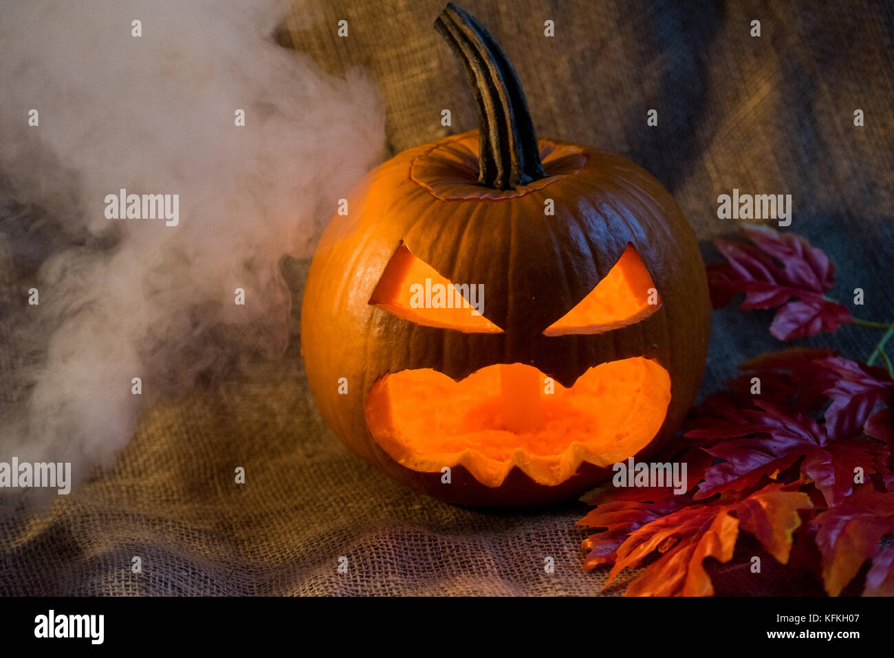 Scary jack-o-lantern, light inside and red leaves Stock Photo - Alamy