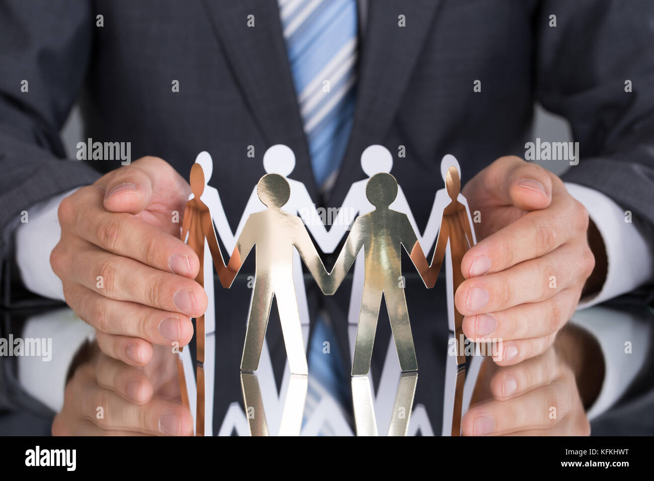 Businessman protecting paper people at the table Stock Photo - Alamy