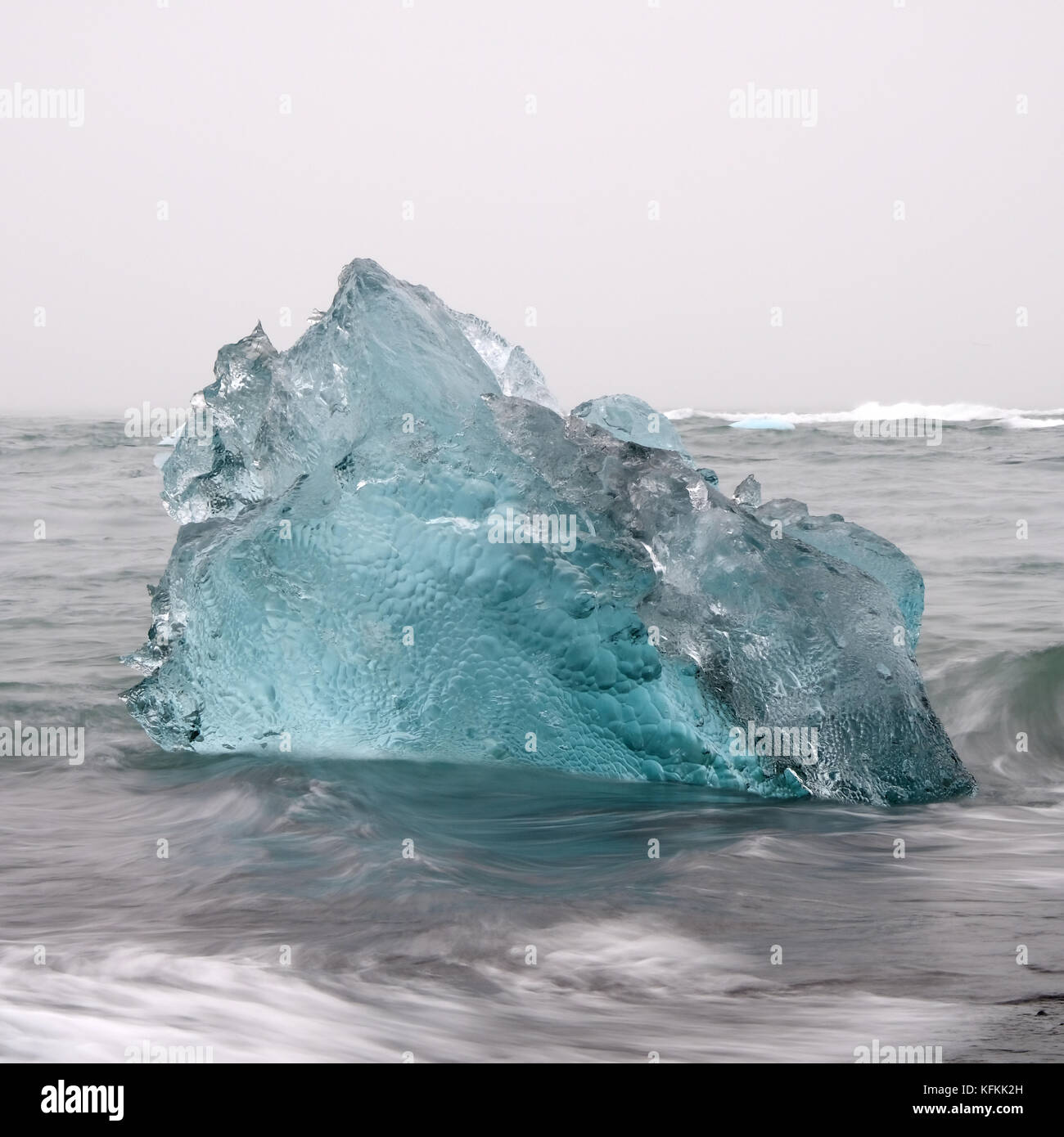 Floating turquoise blue iceberg in glacial waters and waves on a grey ...