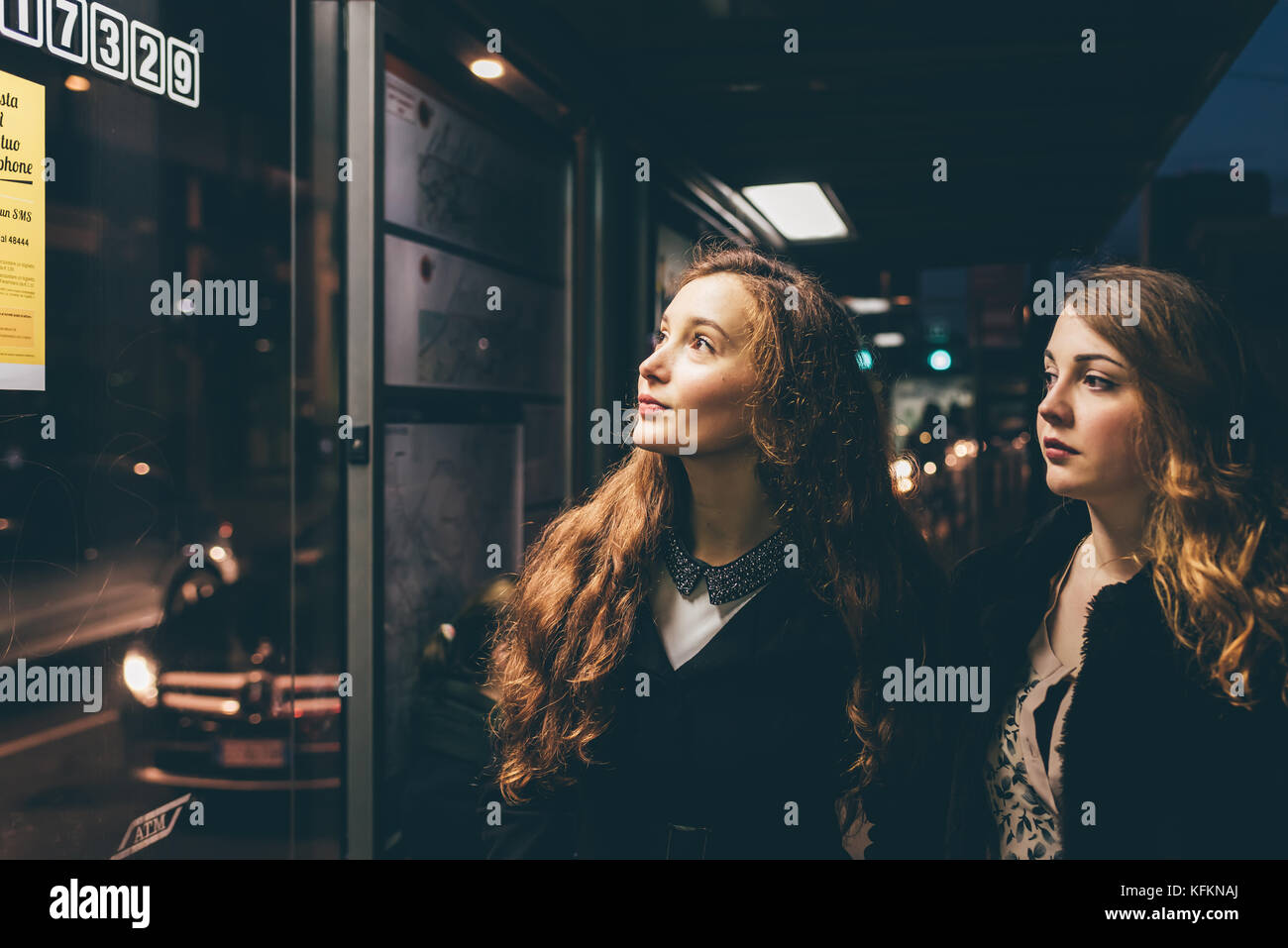two young women friends standing outdoor checking time table at bus ...