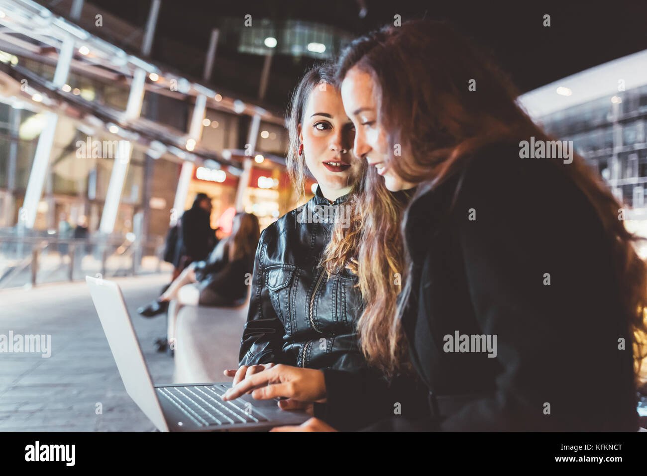 two young women outdoor city night using computer laptop - business ...