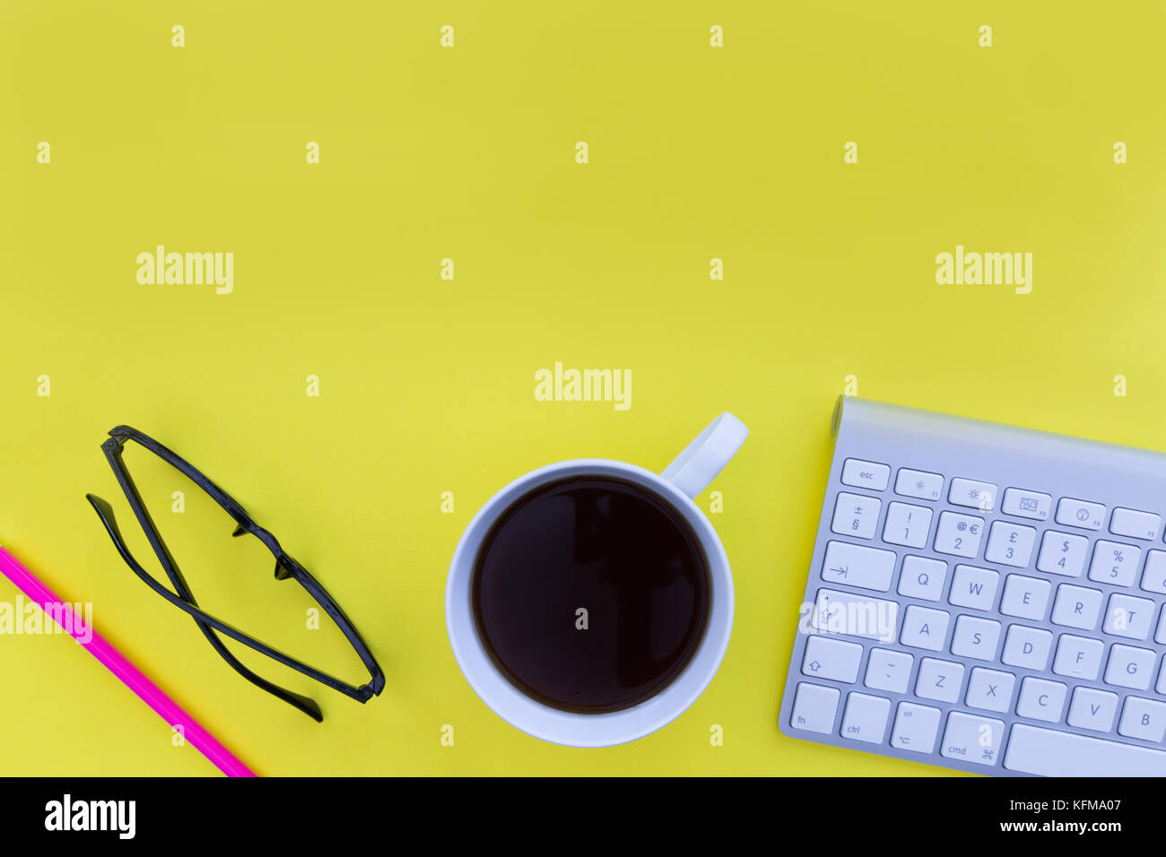 Computer keyboard coffee cup and eyeglasses on bright yellow background ...