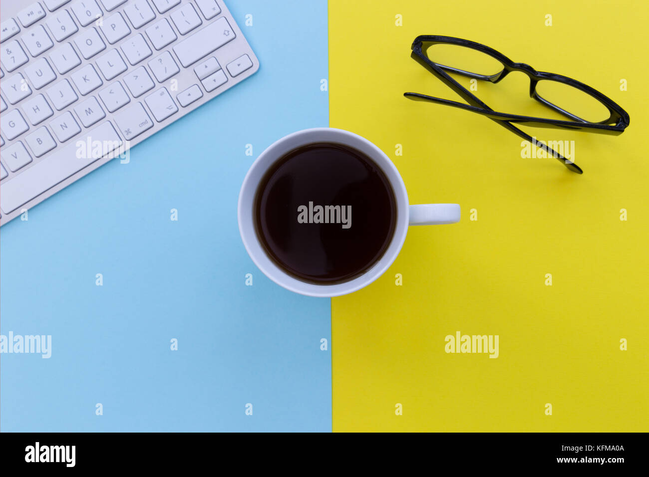 Computer keyboard and coffee cup overhead on bright blue and yellow ...