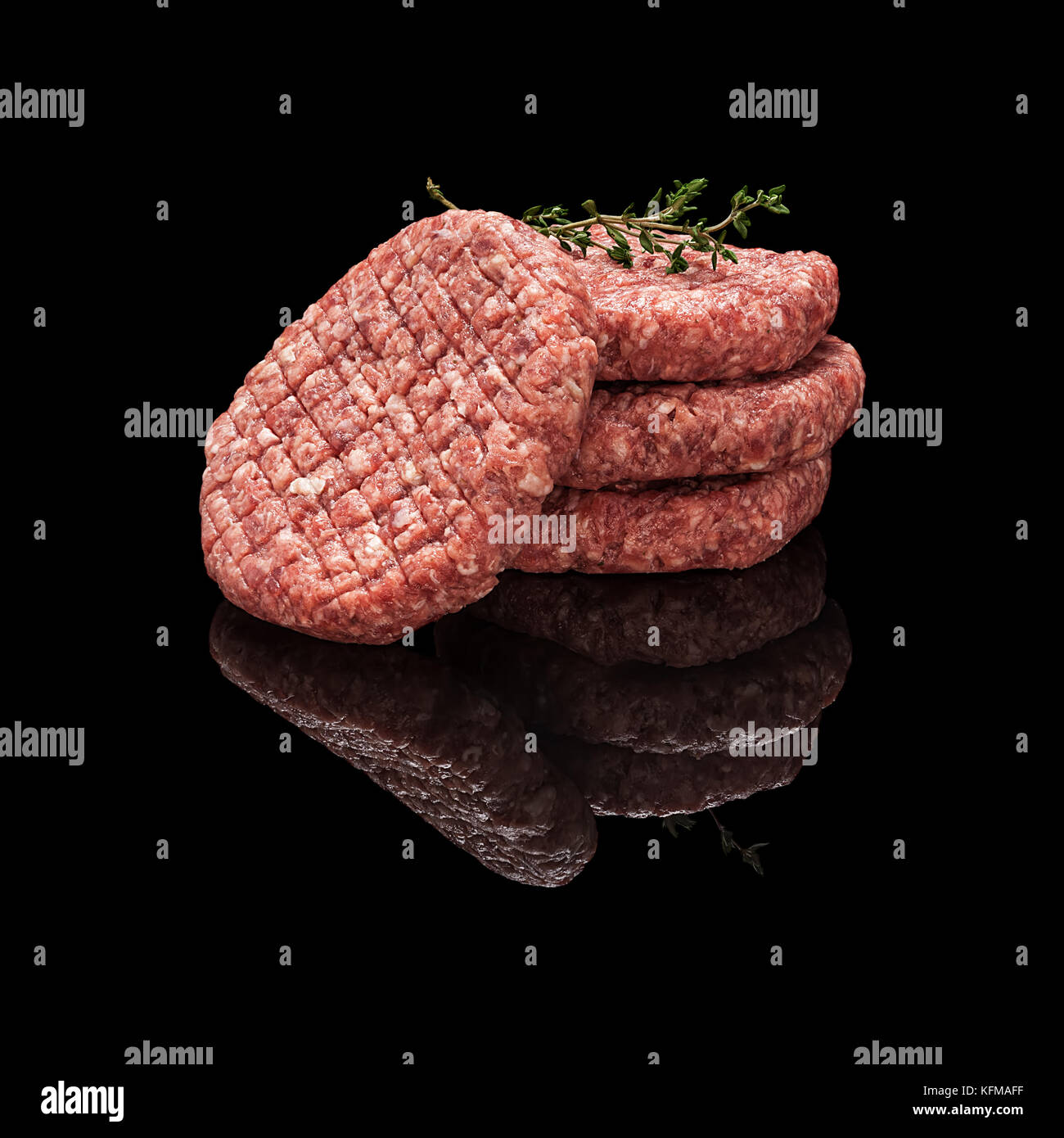 Stack of raw beef patties with branch of thyme isolated on black glossy ...