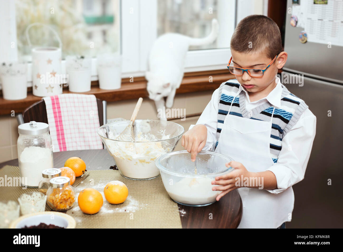 7-year-old boy mixing ingredients for baking a cake. White cat in the ...