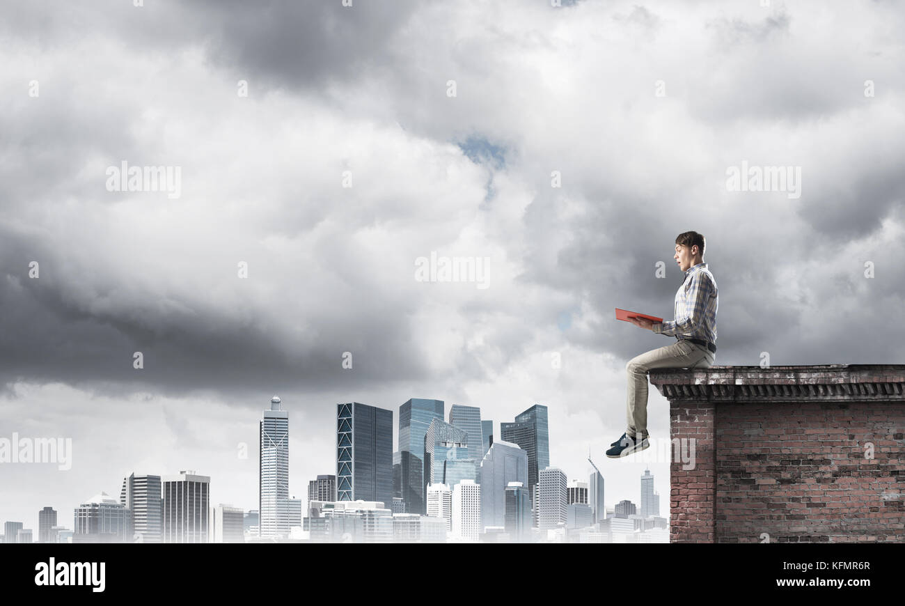 Man on roof edge reading book and cityscape at background Stock Photo ...