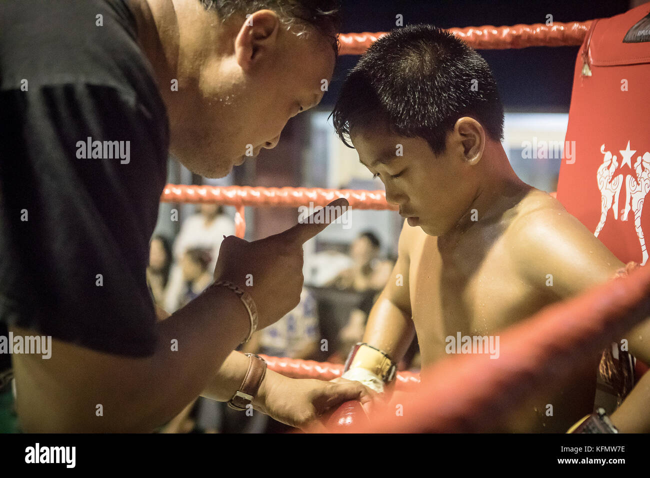 Young Thai boxing sitting in the conner of the ring, advised by his ...