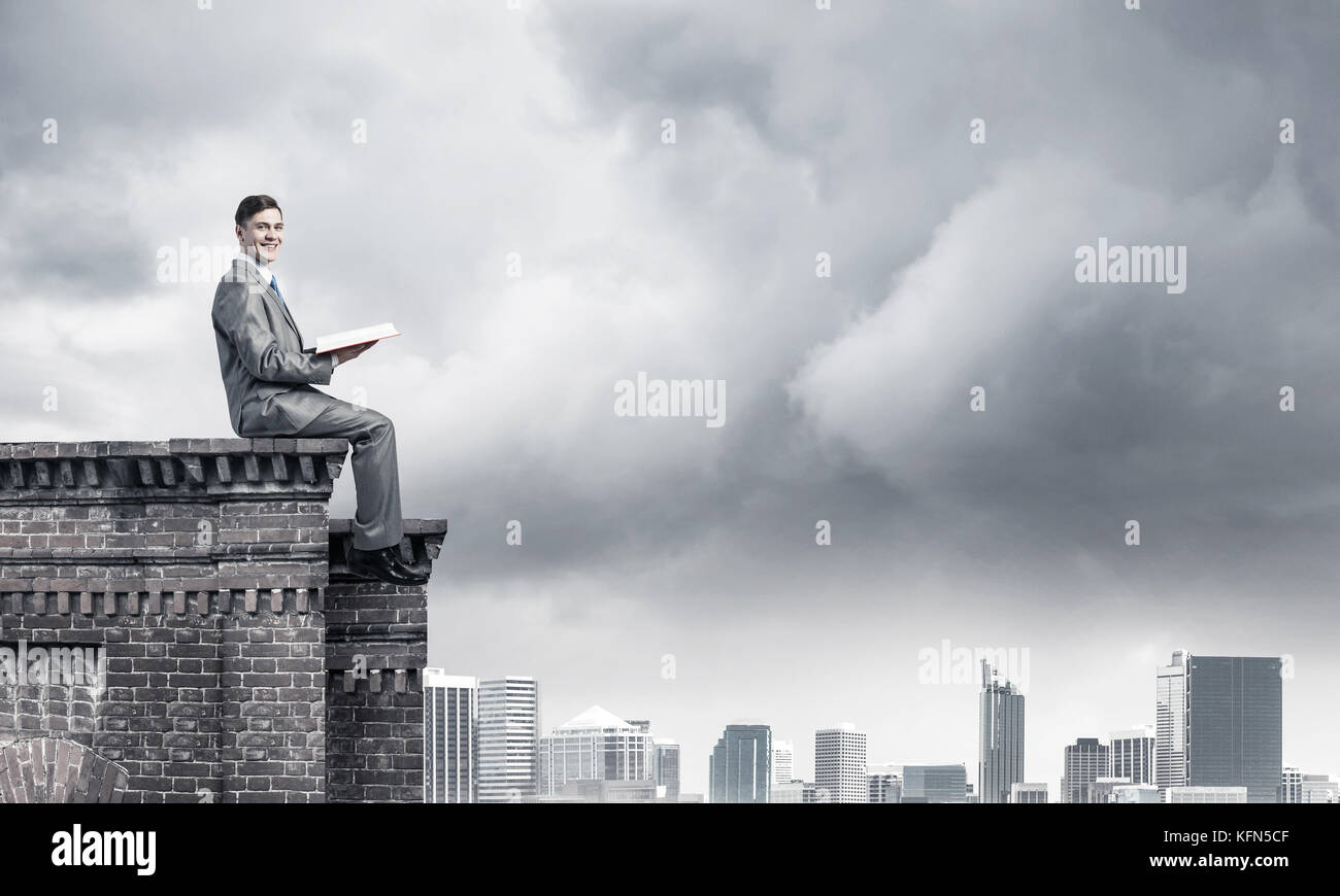 Man on roof edge reading book and cityscape at background Stock Photo ...