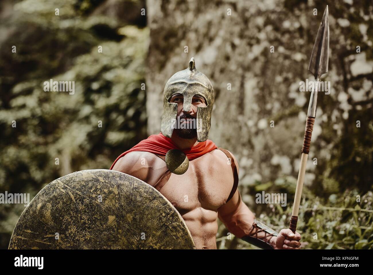 Confident strong man in gladiator armor holding metal heavy shield and ...