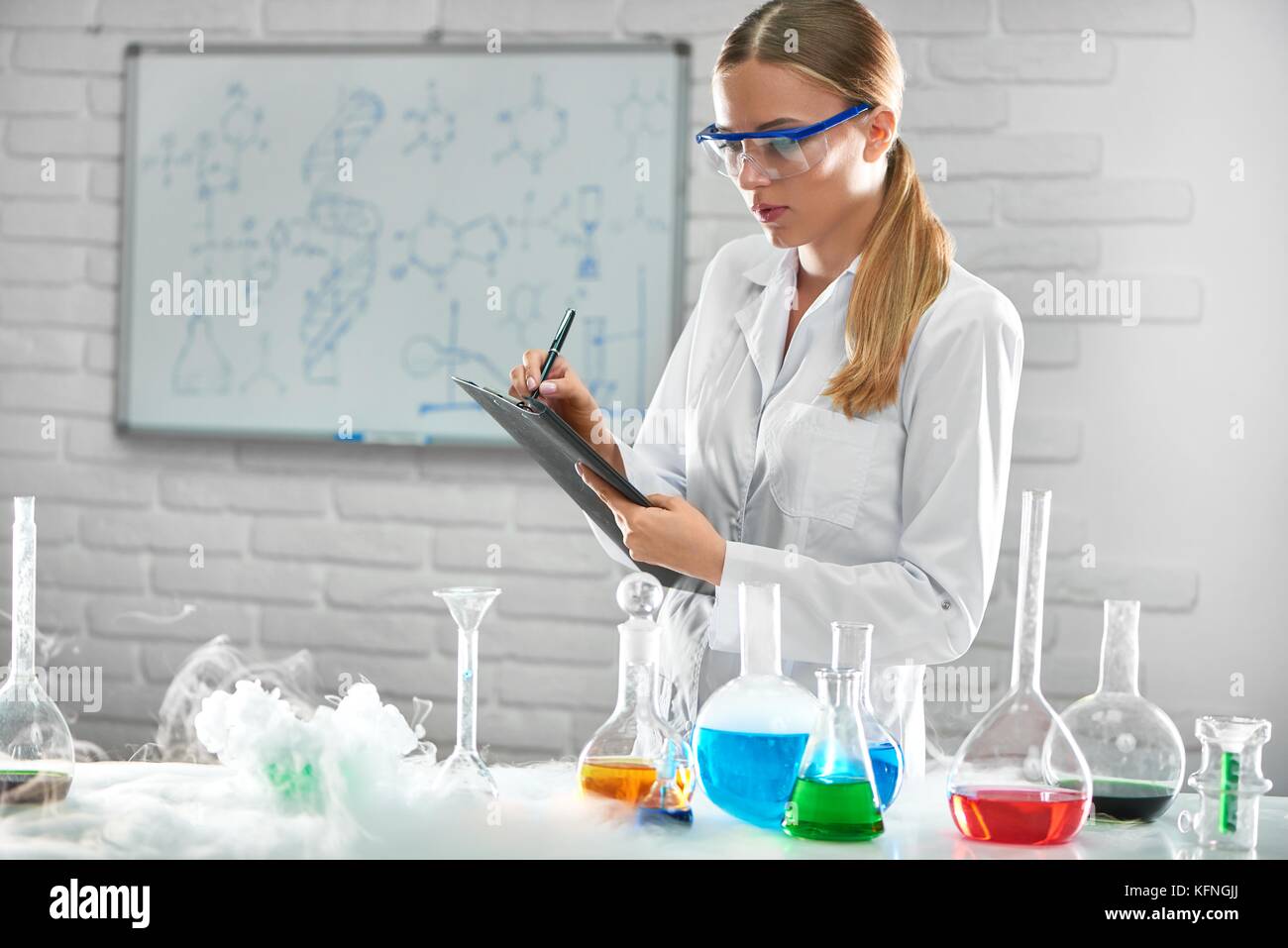 Attractive female scientist making notes on her clipboard after ...