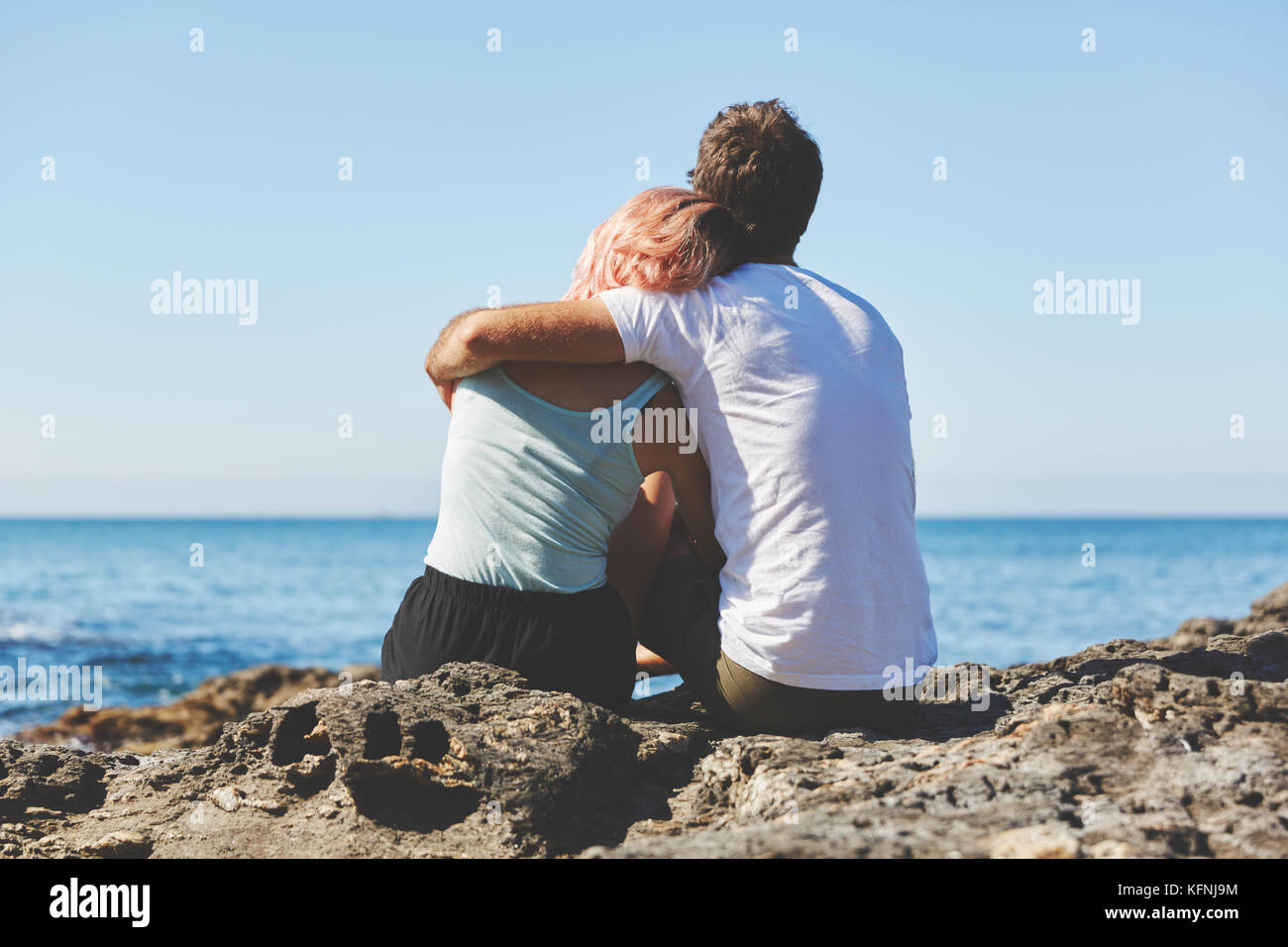 Back portrait of couple sitting on rock hugging each other Stock Photo ...