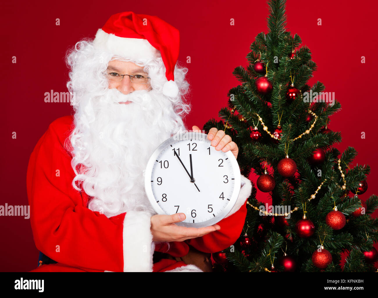 Portrait of a happy santa holding clock over red background Stock Photo ...