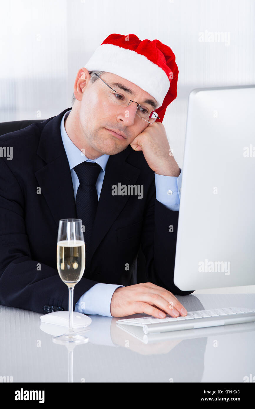 Sad Businessman Wearing Santa Hat Sitting In Front Of Computer With ...