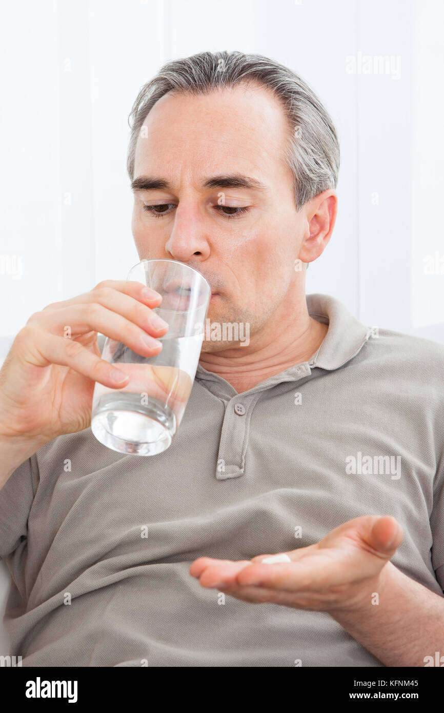 Ill man taking medication sitting up holding a glass of water looking ...