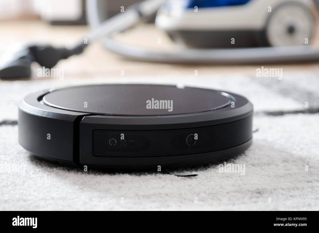 Robotic vacuum cleaner working on carpet. Traditional vacuum cleaner in ...