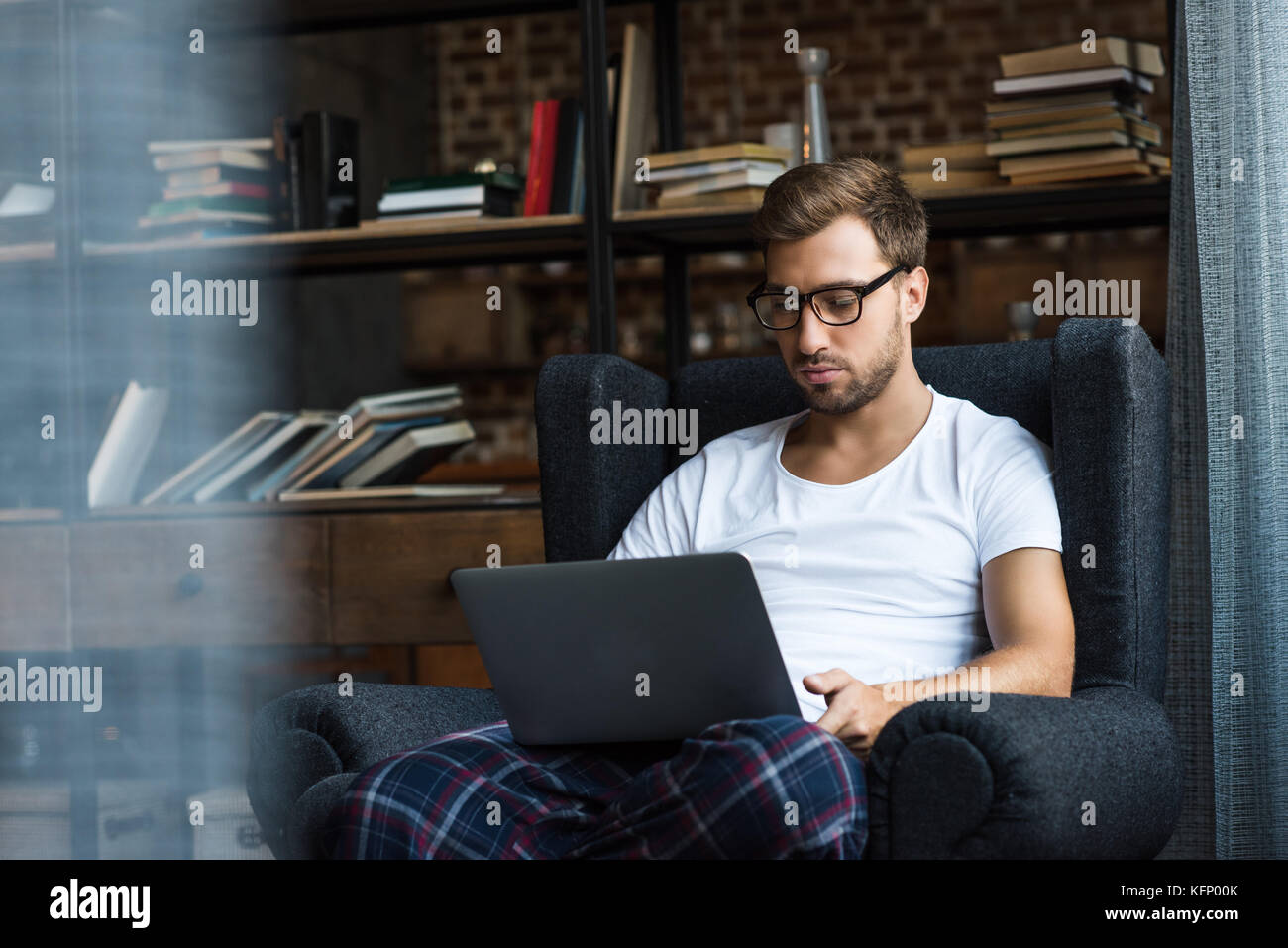 Young man sitting in armchair using laptop hi-res stock photography and ...