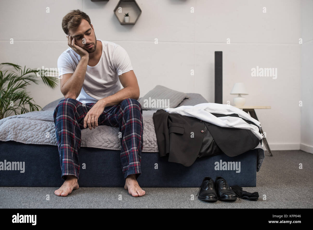 Sleepy man sitting on bed Stock Photo - Alamy