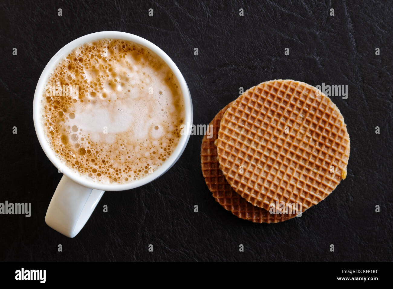 Milky frothy coffee in white mug next to a couple of round waffle ...