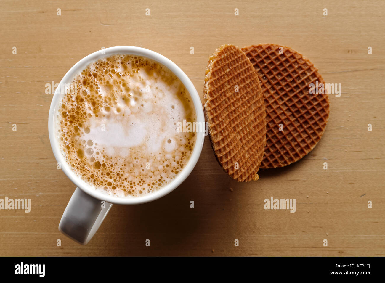 Milky frothy coffee in white mug next to a couple of round waffle ...