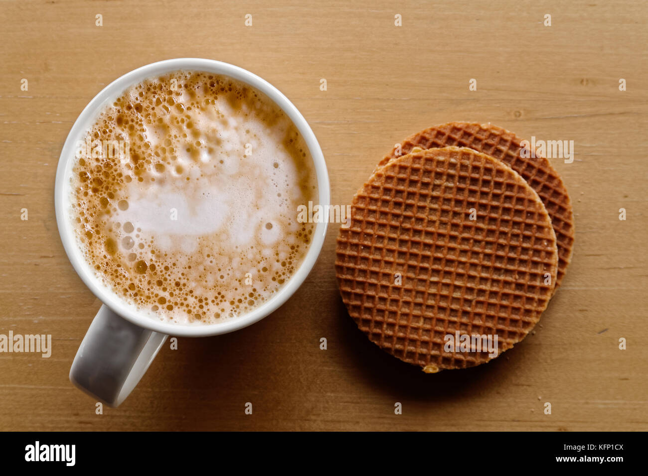 Milky frothy coffee in white mug next to a couple of round waffle ...