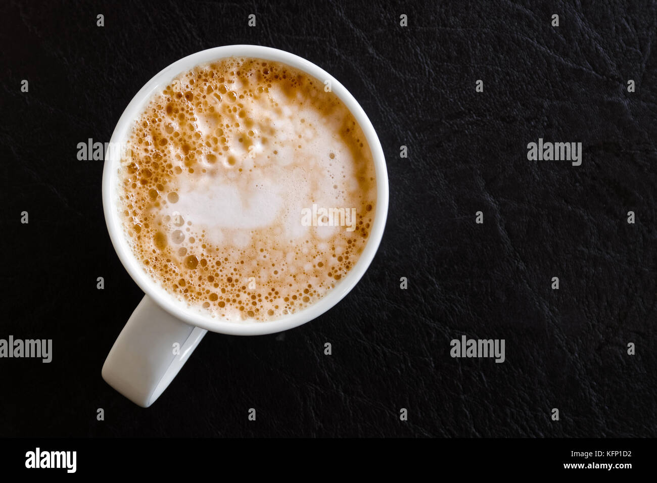 Milky frothy coffee in white mug isolated on black leather from above ...