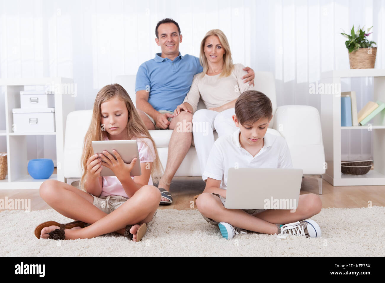 Children On The Carpet Using Tablet And Laptop With Parents Behind Them ...