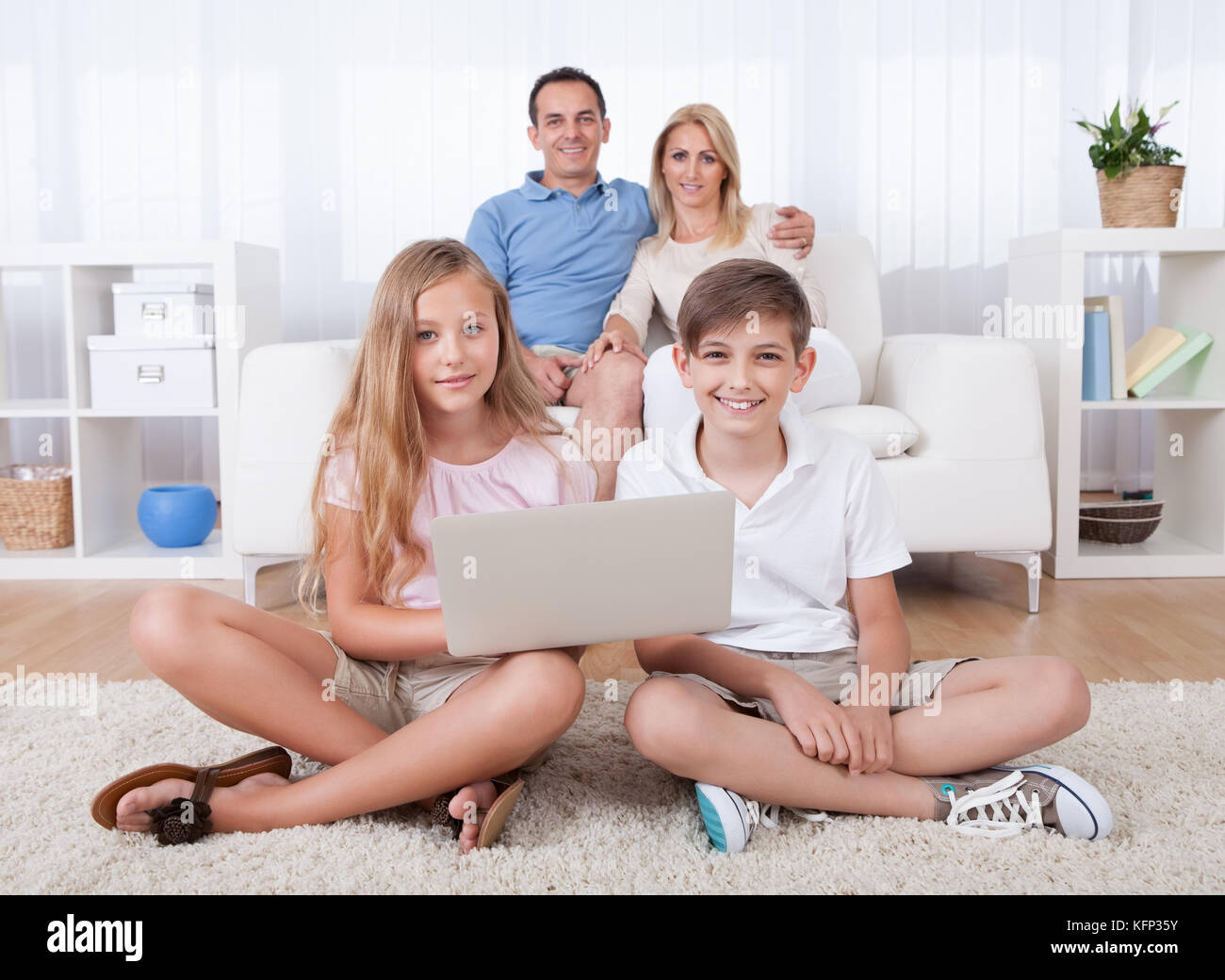 Children On The Carpet Using Tablet And Laptop With Parents Behind Them ...