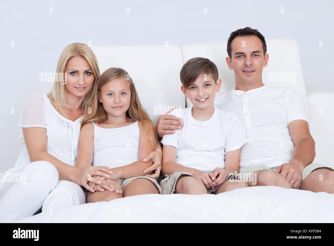 Portrait Of Happy Family With Two Children Sitting On Bed In Bedroom ...