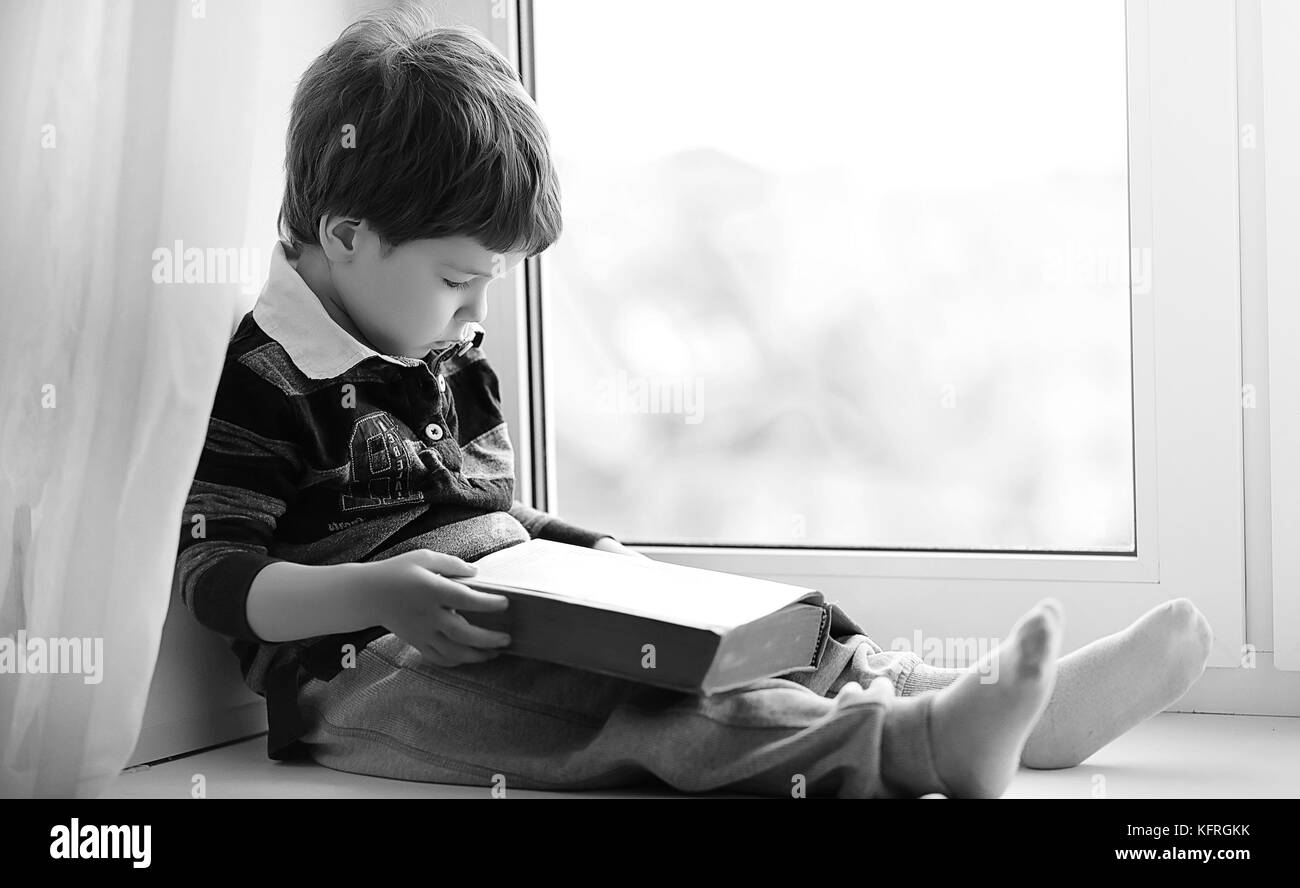 The little boy is reading a book. The child sits at the window a Stock ...