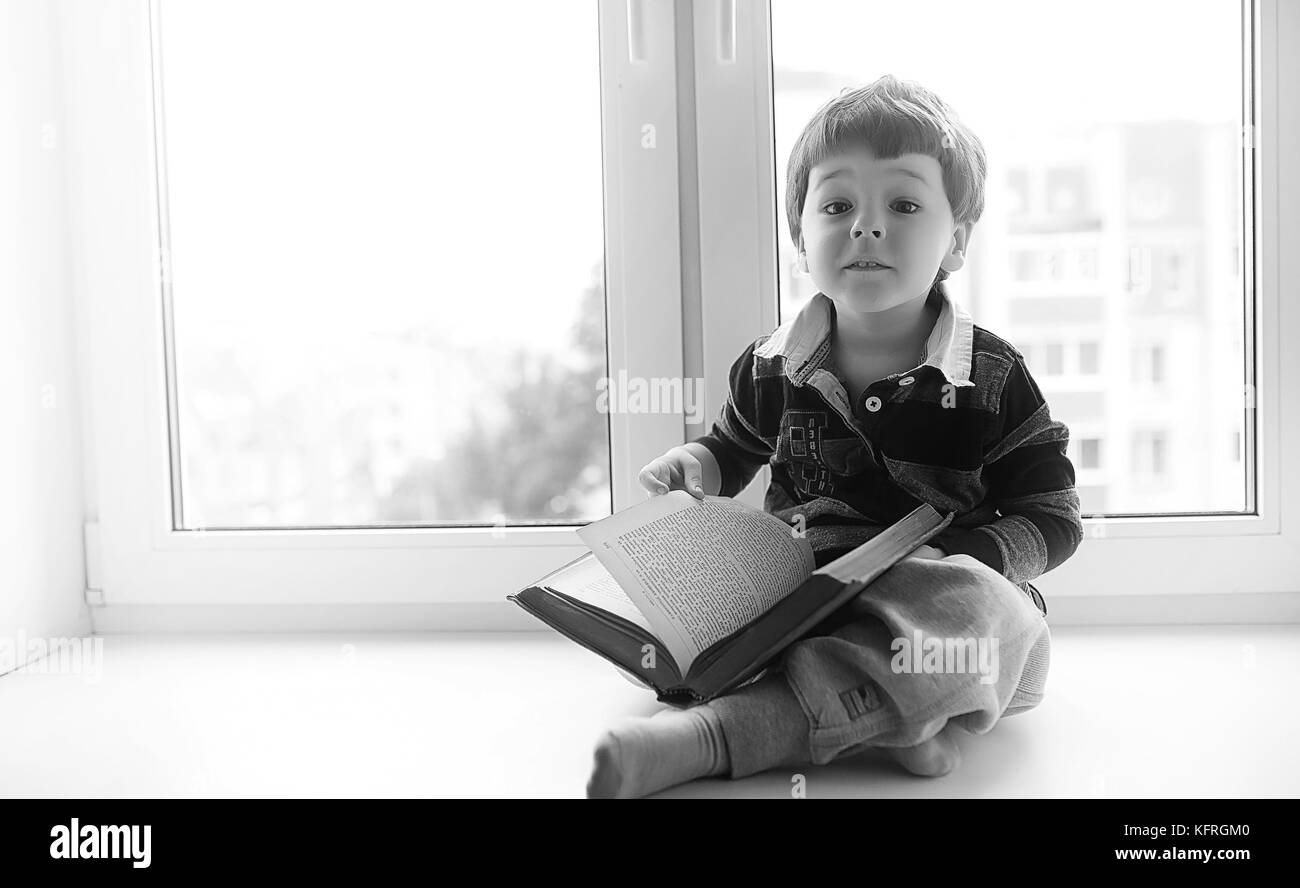 The little boy is reading a book. The child sits at the window a Stock ...