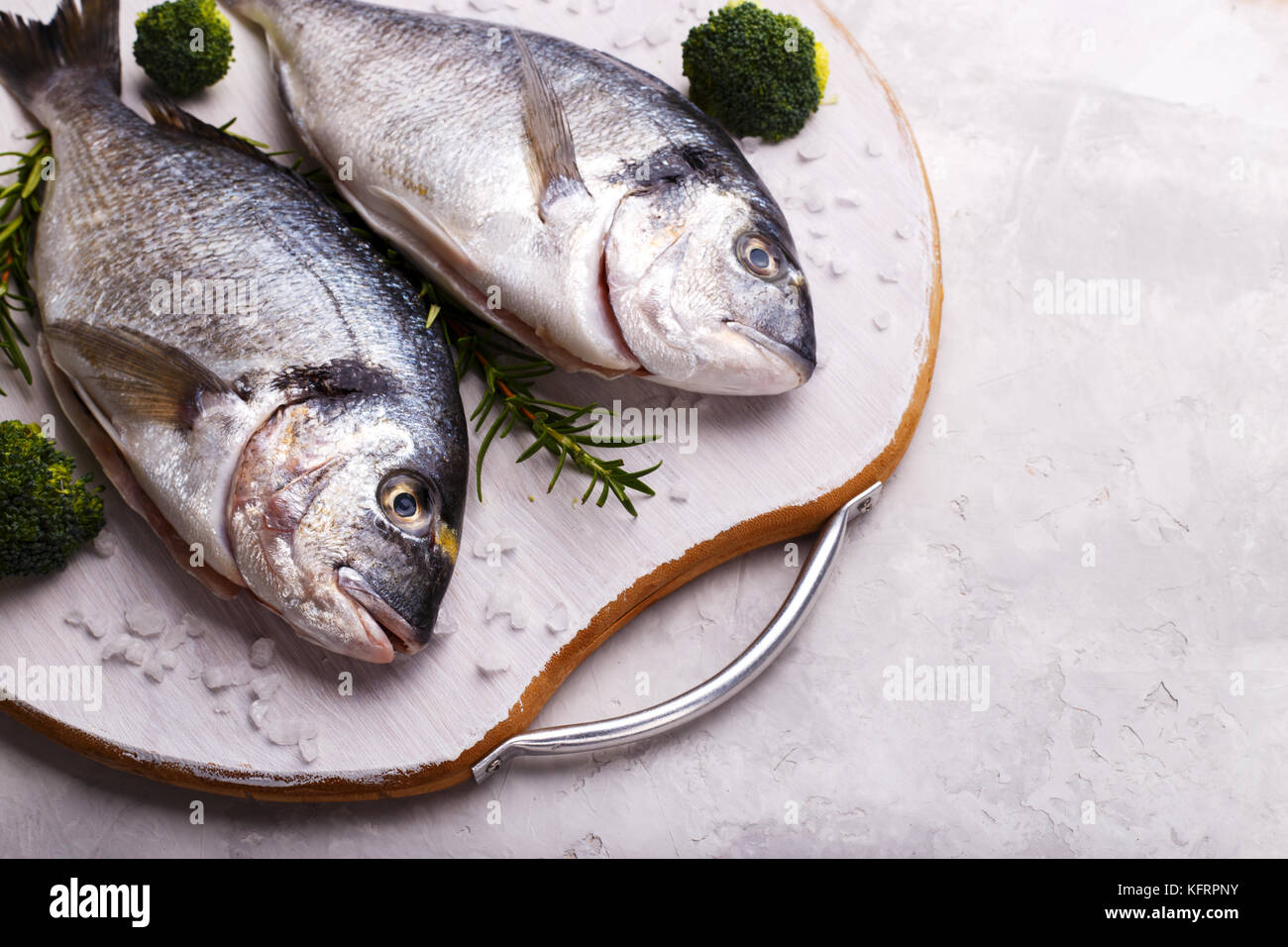 Raw sea bream fish with rosemary and broccoli on white gray stone ...