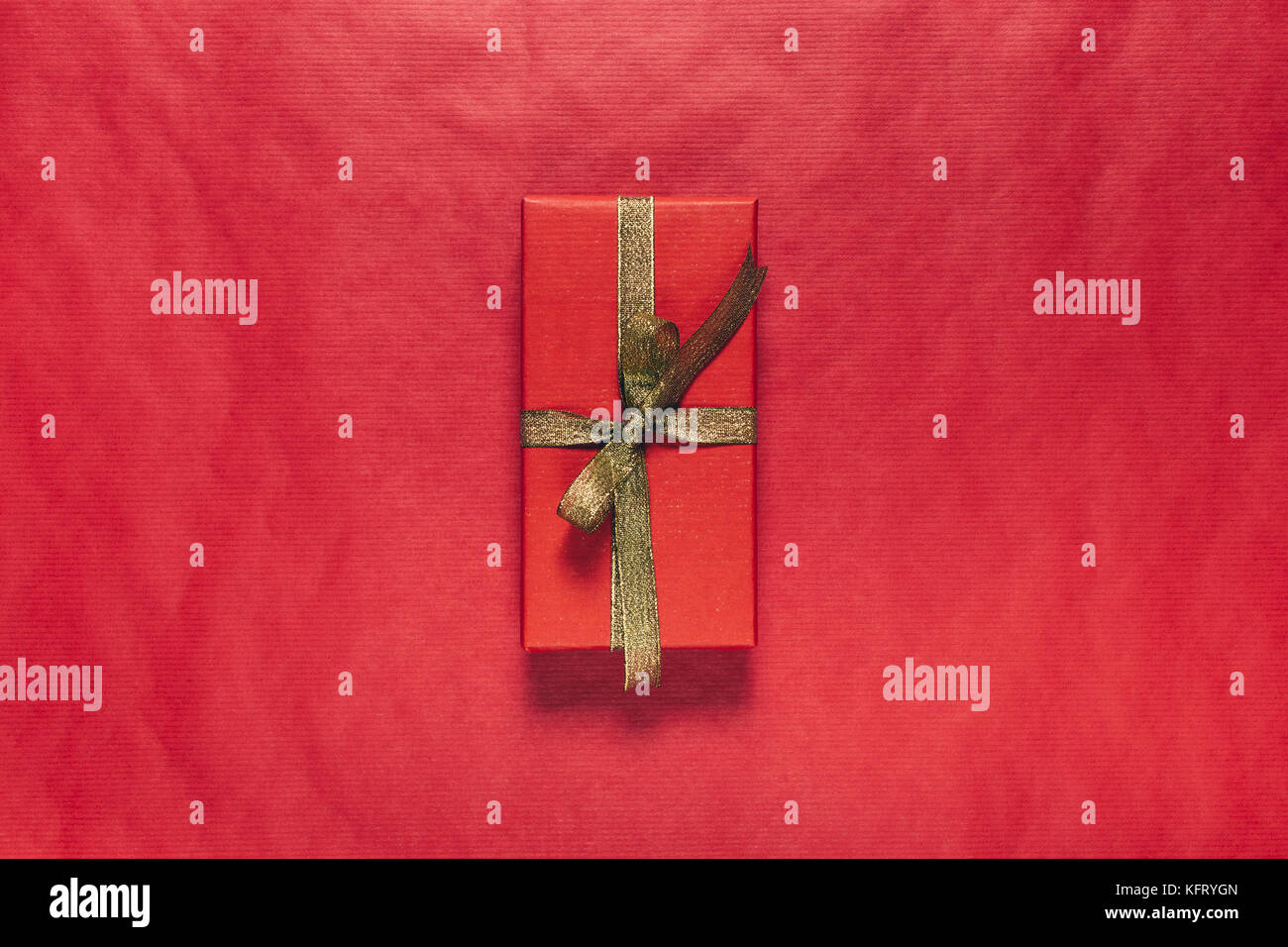 Gift box in wrapping paper with golden ribbon on red background, top ...
