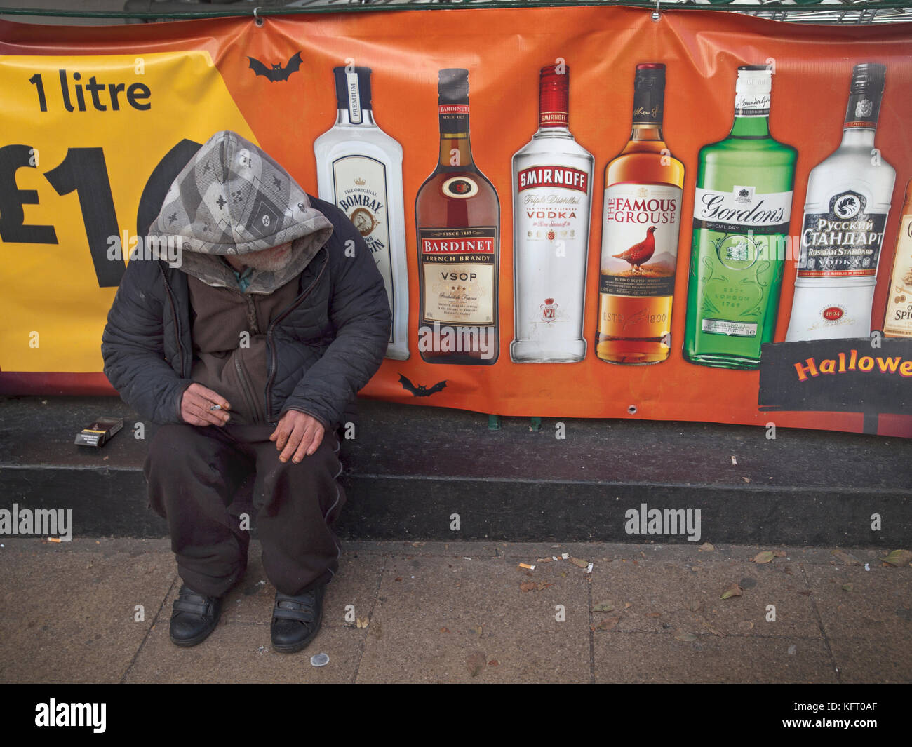 A rough sleeper sits on the pavement by adverts for alcohol in Brighton ...