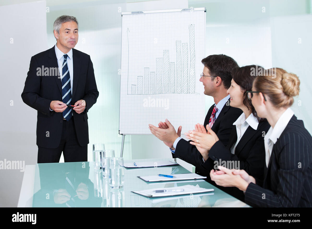 Diverse business colleagues seated around a table clapping after a ...