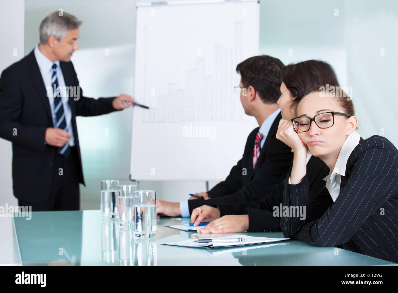 Bored businesswoman sleeping in a meeting as her colleague who is ...