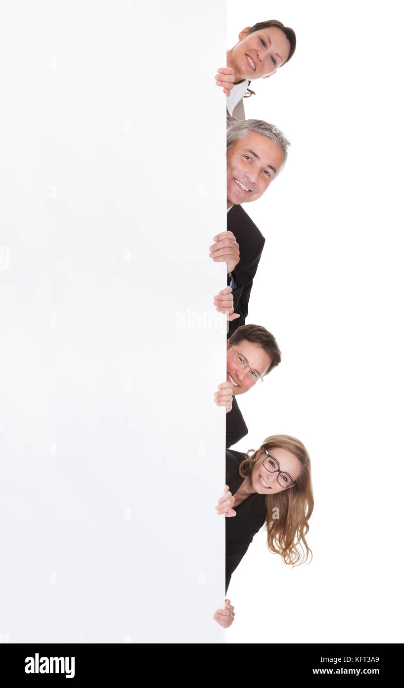 Four diverse professional businesspeople peering around the edge of a ...