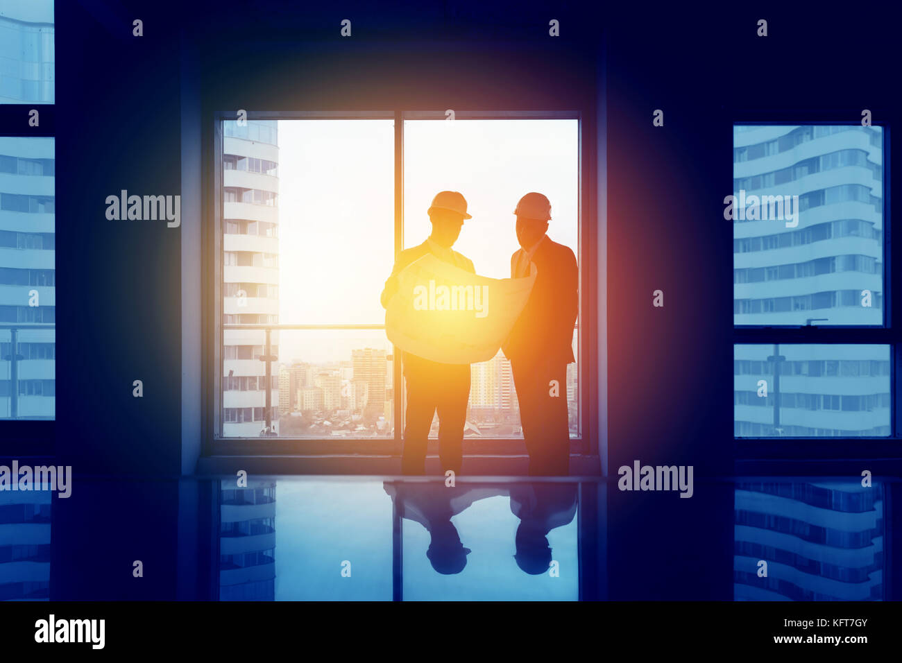 Silhouettes of two engineers with big blueprint in hands are discussing ...