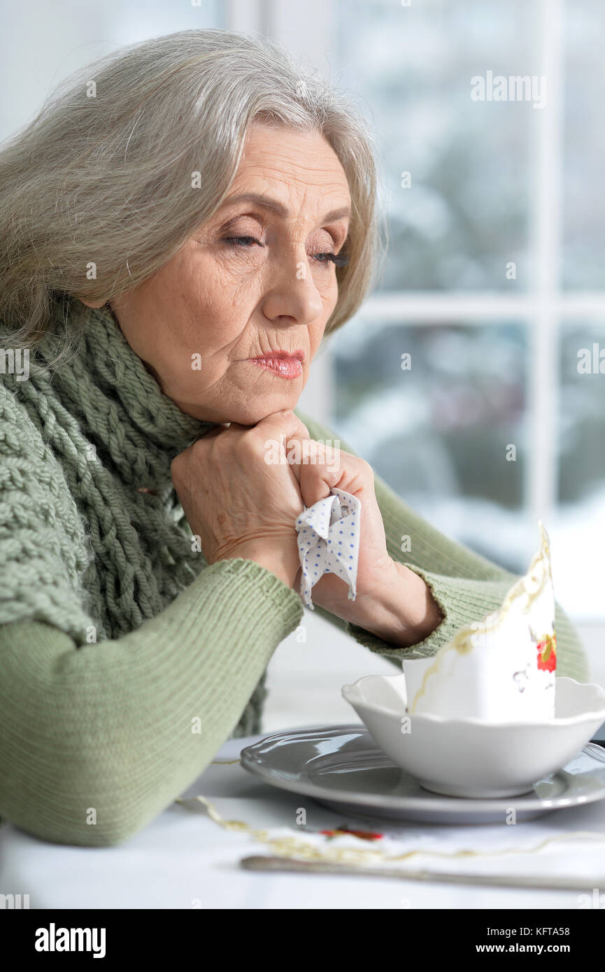 Portrait of sad senior woman sitting at table Stock Photo - Alamy