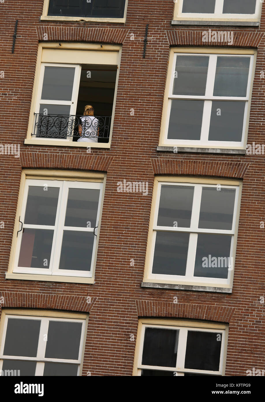 young blonde girl at the apartment building window in an european city ...