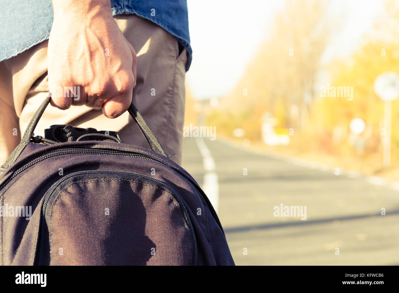 Male hand holding backpack waiting for pickup on a sunny autumn day on ...