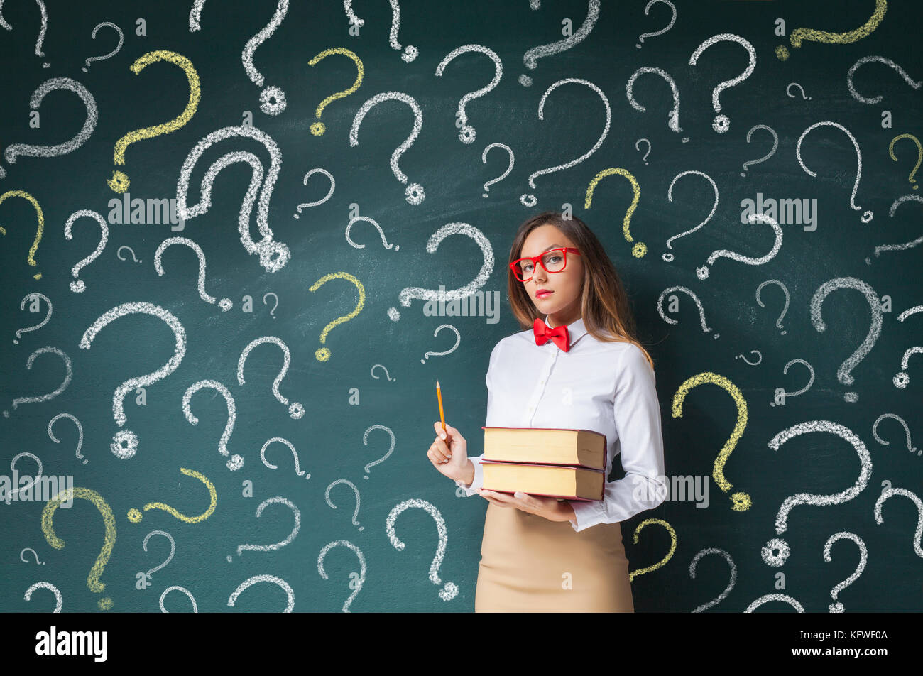 Young teacher standing near blackboard and question mark drawn in chalk ...
