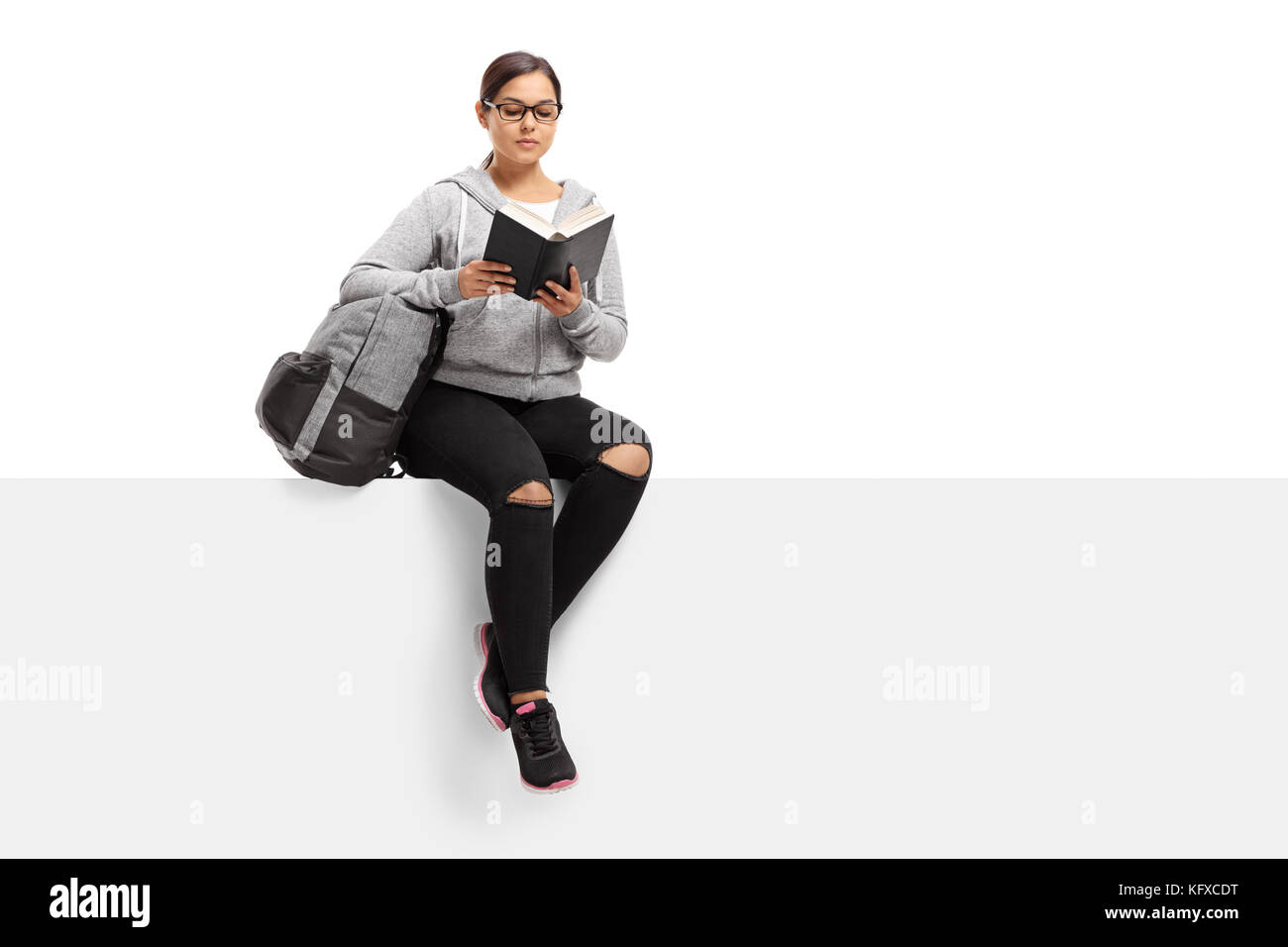 Female teenage student seated on a panel reading a book isolated on ...