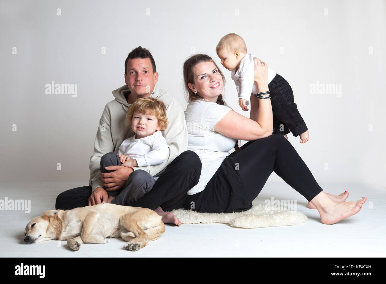 Two generation family studio portrait with dog on grey and white ...