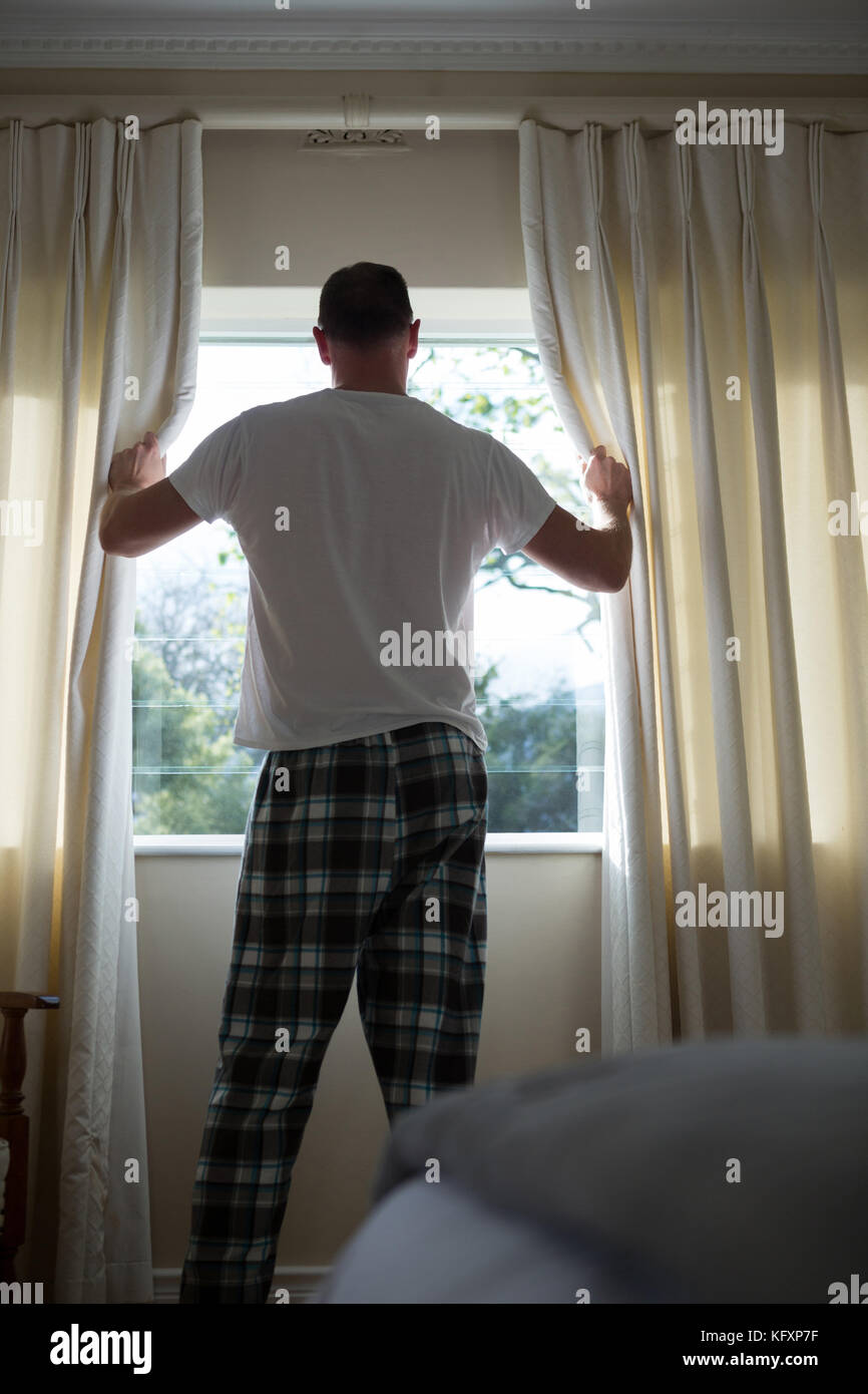 Rear view of man opening window curtain in bedroom Stock Photo - Alamy