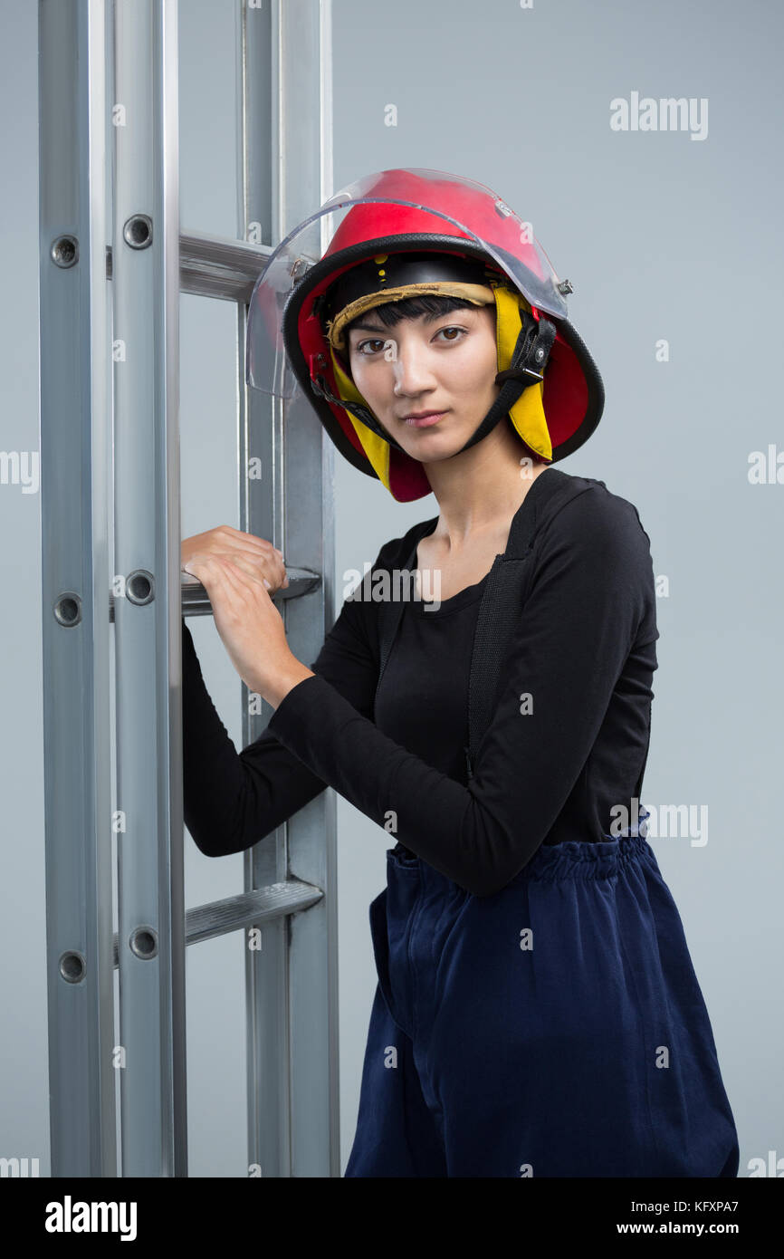 Portrait of female architect holding ladder against white background ...