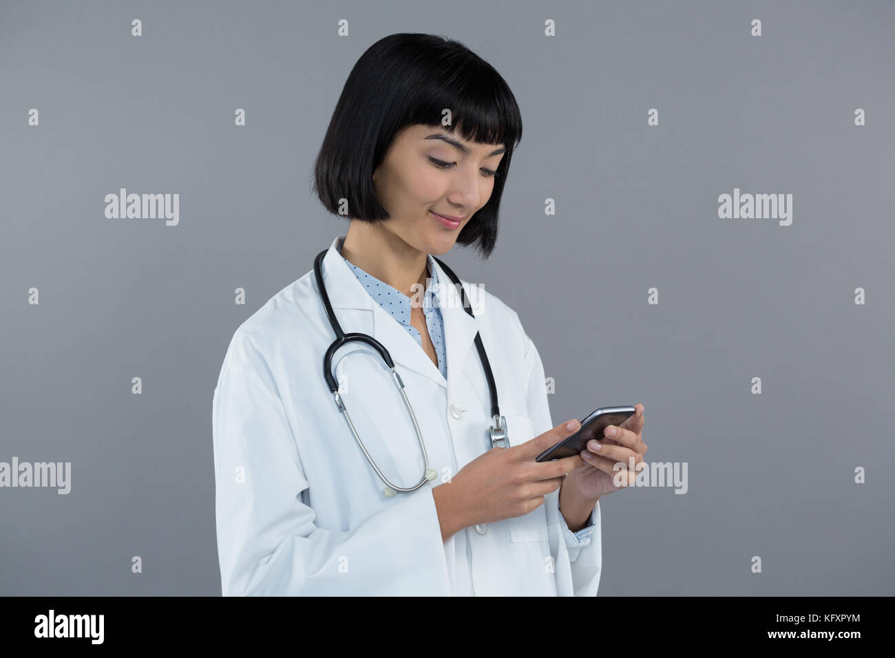 Smiling doctor using mobile phone against grey background Stock Photo ...