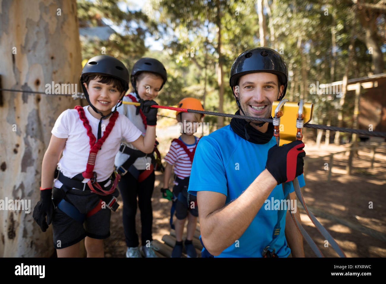 Smiling kids and instructor getting ready to zip line in park Stock ...