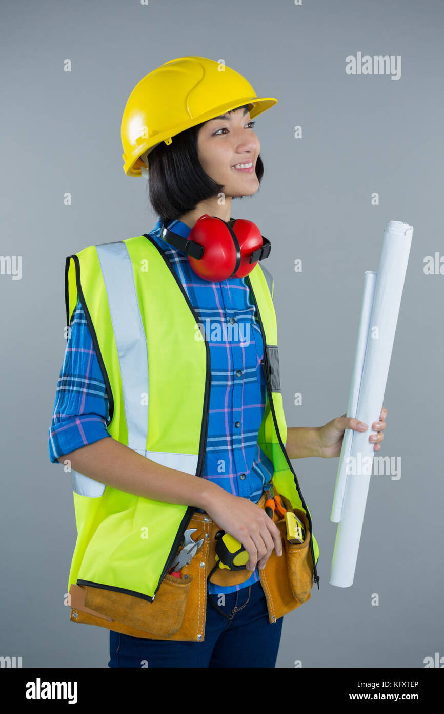 Thoughtful female architect holding blueprint against grey background ... Thoughtful female architect holding blueprint against grey background ...